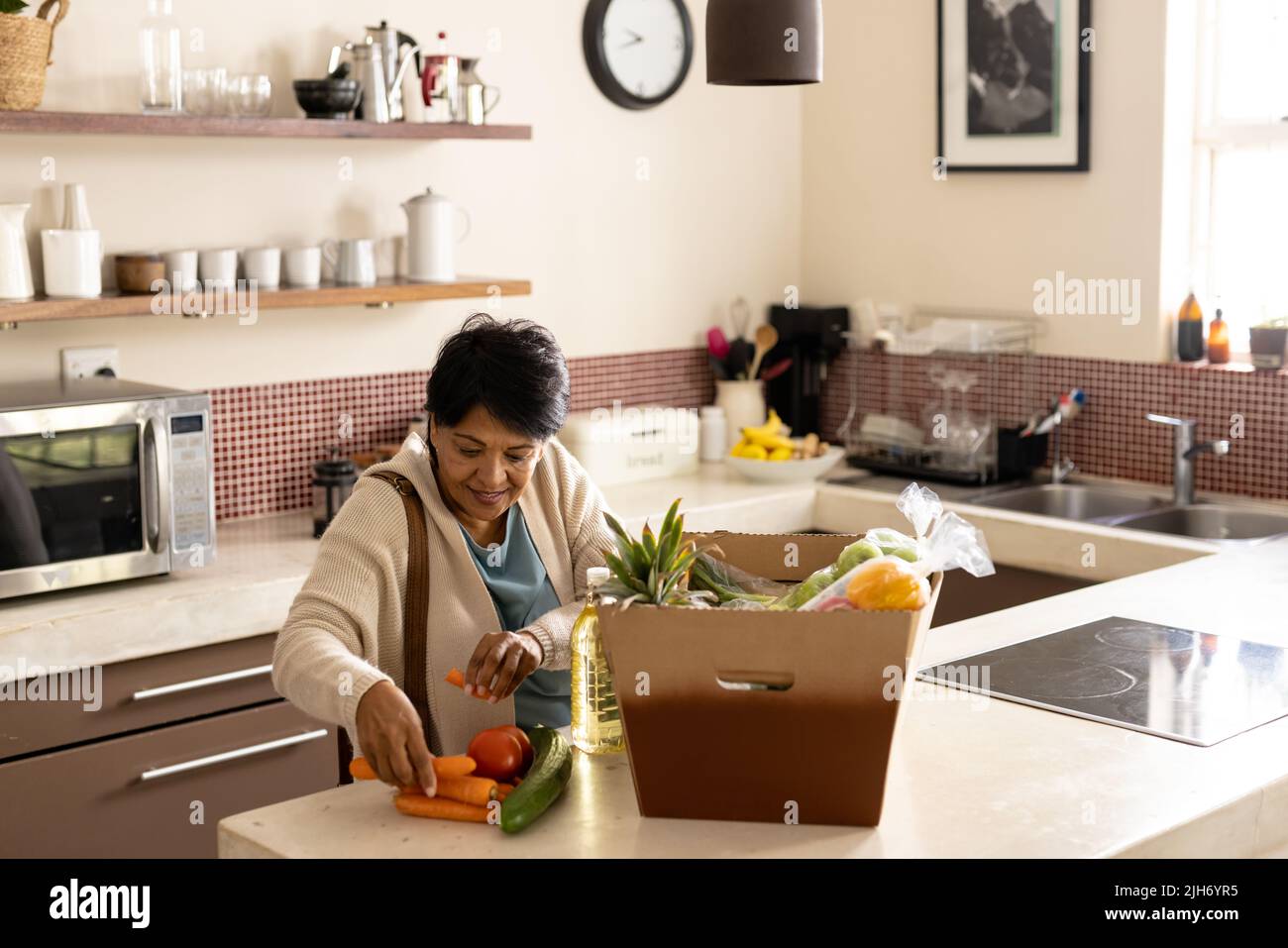 Biracial mature woman unpacking fresh vegetables and fruits from ...