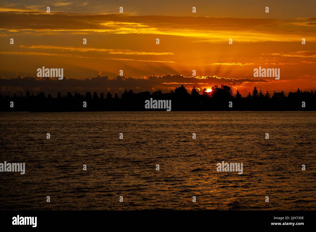 Sun setting over water showing tree lined far share Stock Photo - Alamy