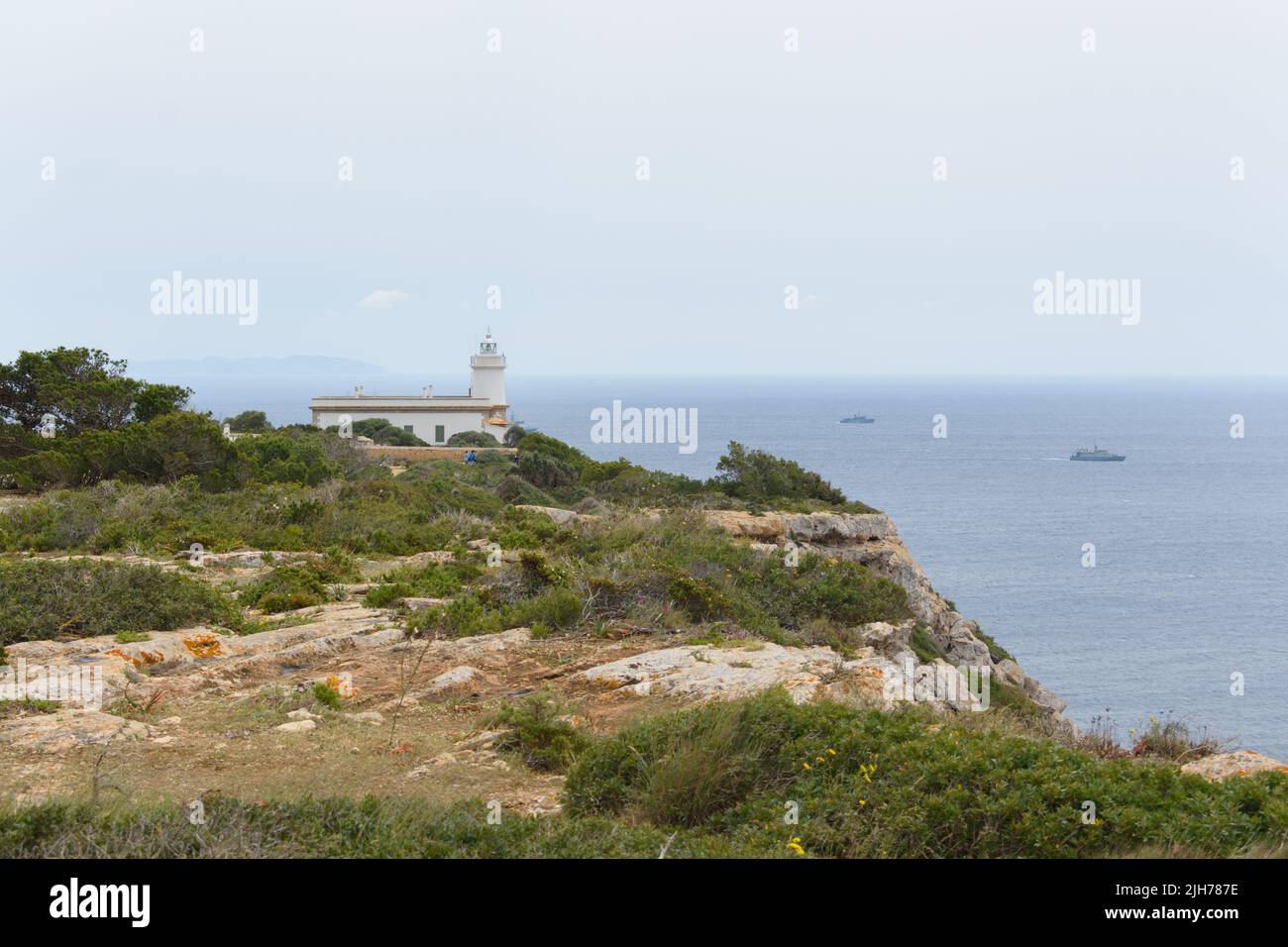 Lighthouse at Far de Cap Blanc in Mallorca, Spain. Naval ships in sea ...
