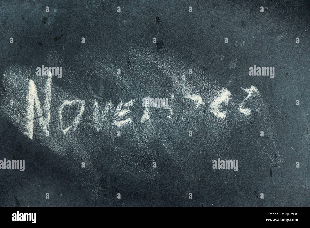 Semi-erased word NOVEMBER on black chalkboard. Handwritten word. Fuzzy ...