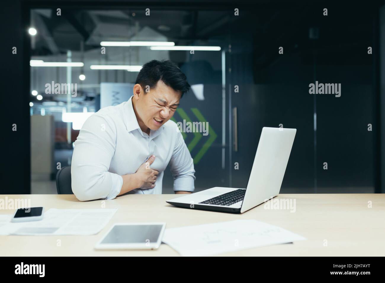 Heart attack at work. A young Asian man, businessman, office worker ...