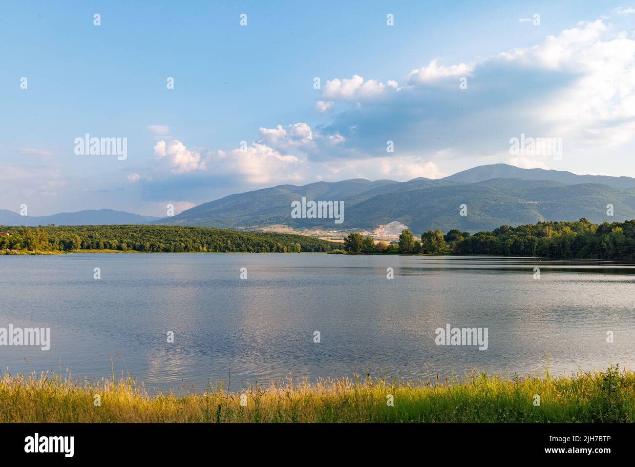 A gleaming wide clear lake reflects bright warm sunlight, against a ...