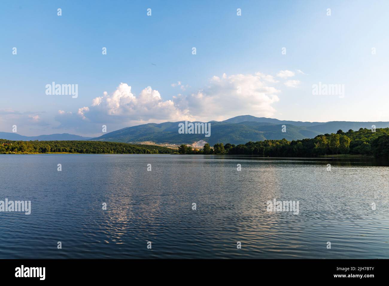 A gleaming wide clear lake reflects bright warm sunlight, against a ...