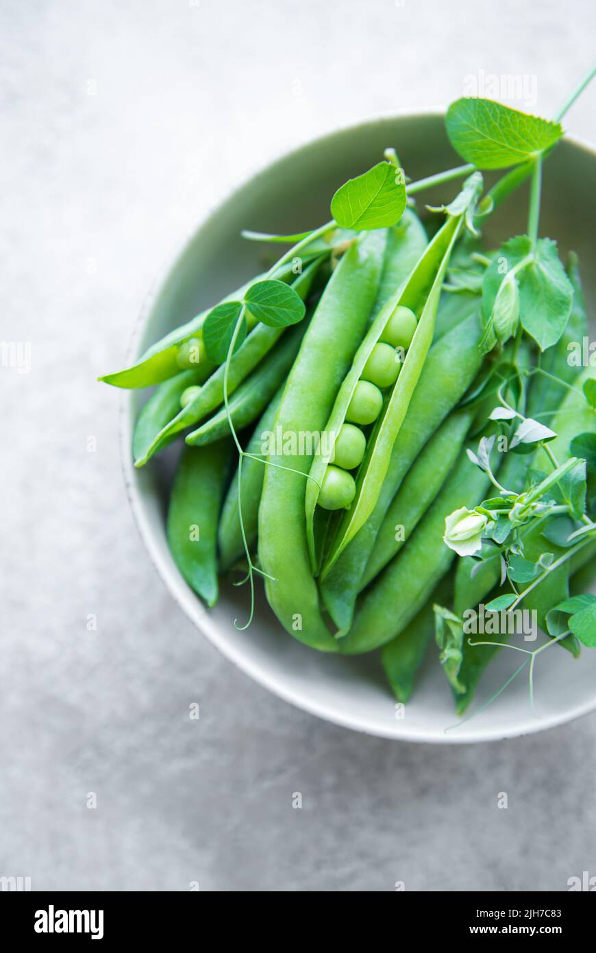 Bowl with young fresh juicy pods of green peas on a concrete background ...