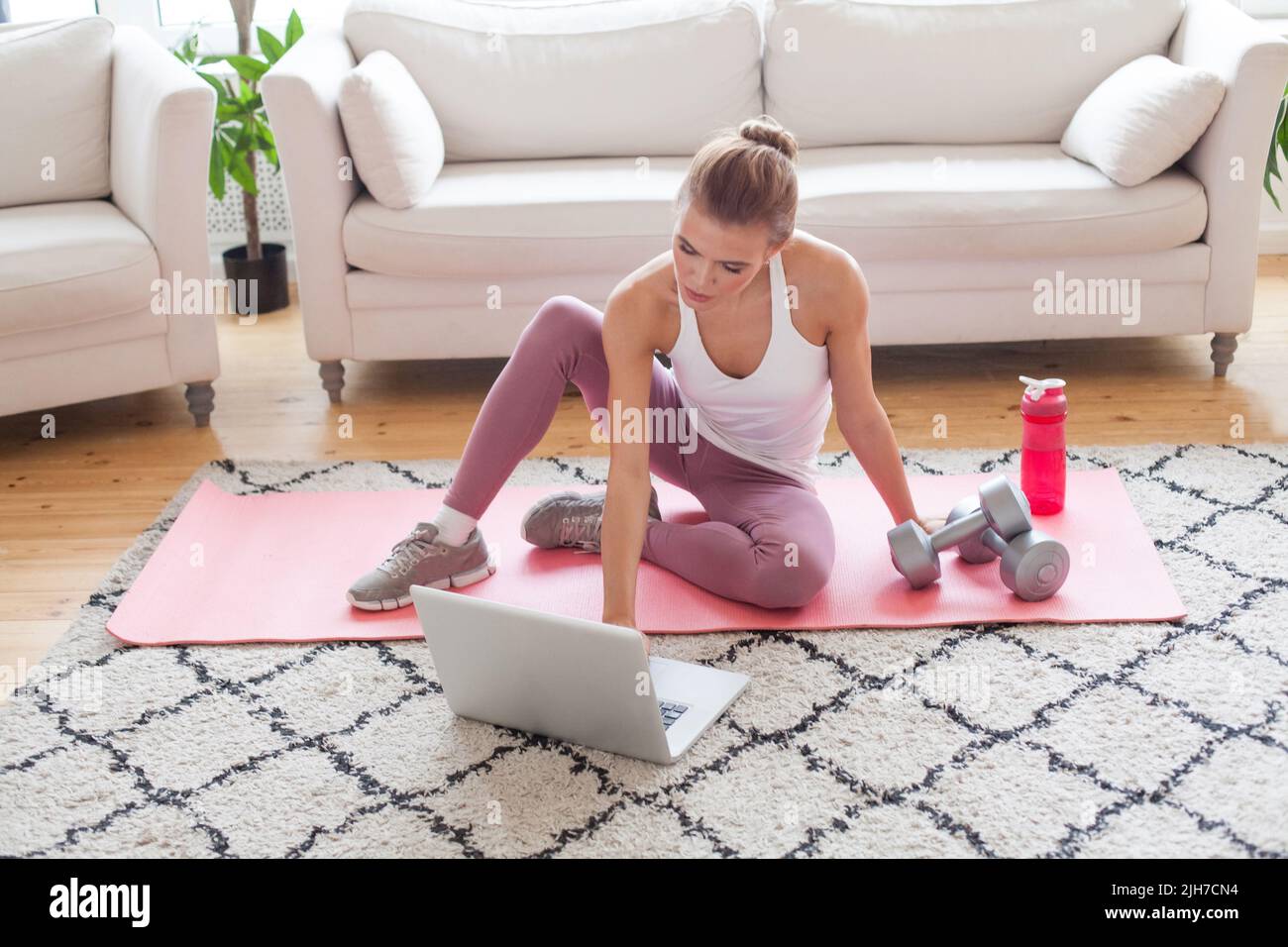 Fit pretty model in activewear sitting on mat using laptop and getting ...
