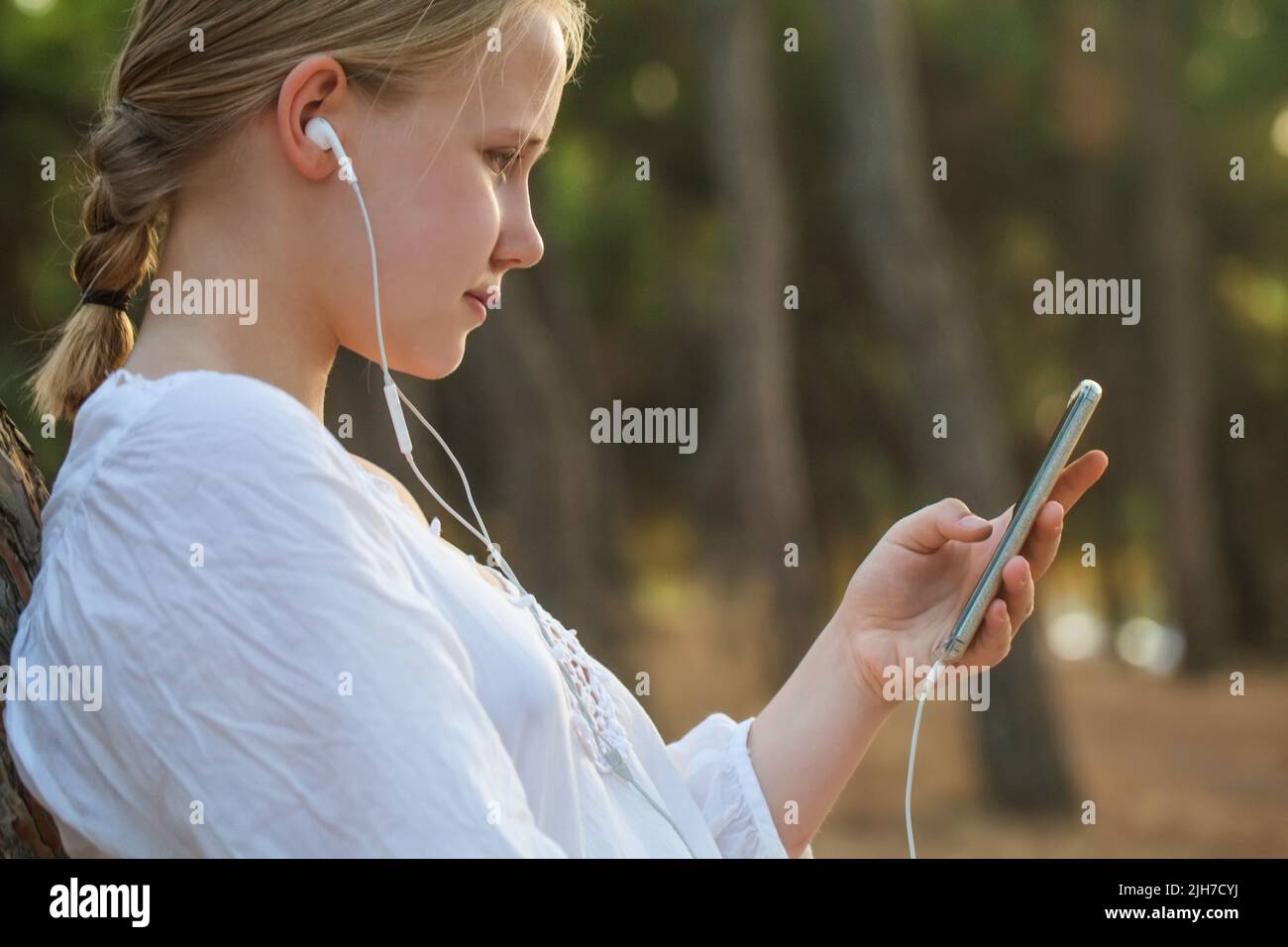 Back view of cute young girl with headphones holding mobile smart phone ...