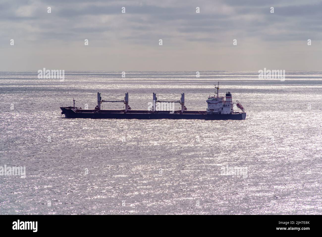 Large industrial ship sailing in the distance with silver waves from ...