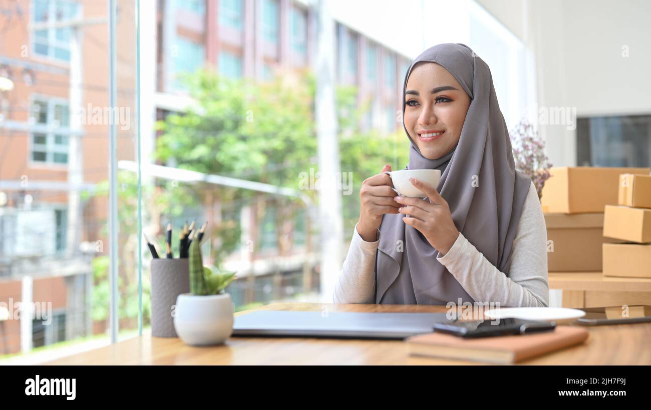 Pleased muslim business woman drinking coffee, thoughtfully looking out ...