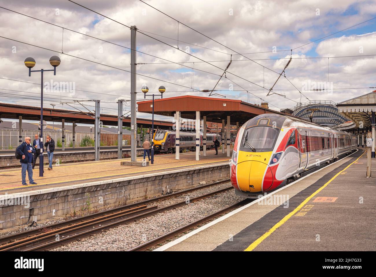 A train waits at a railway station platform and another is at the far ...