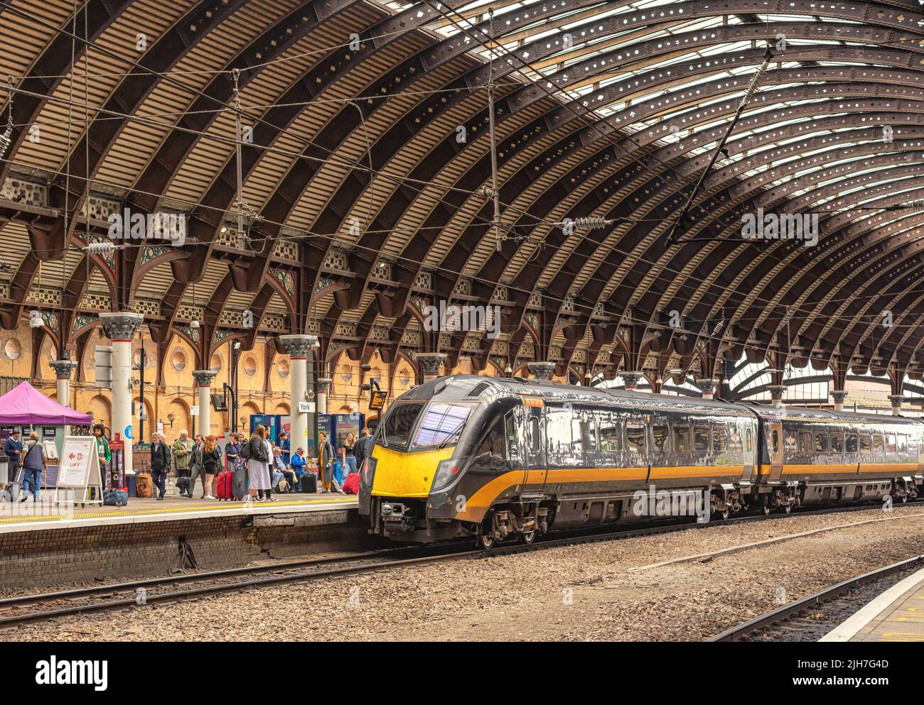 A train rests at a railway station platform under a historic curved ...