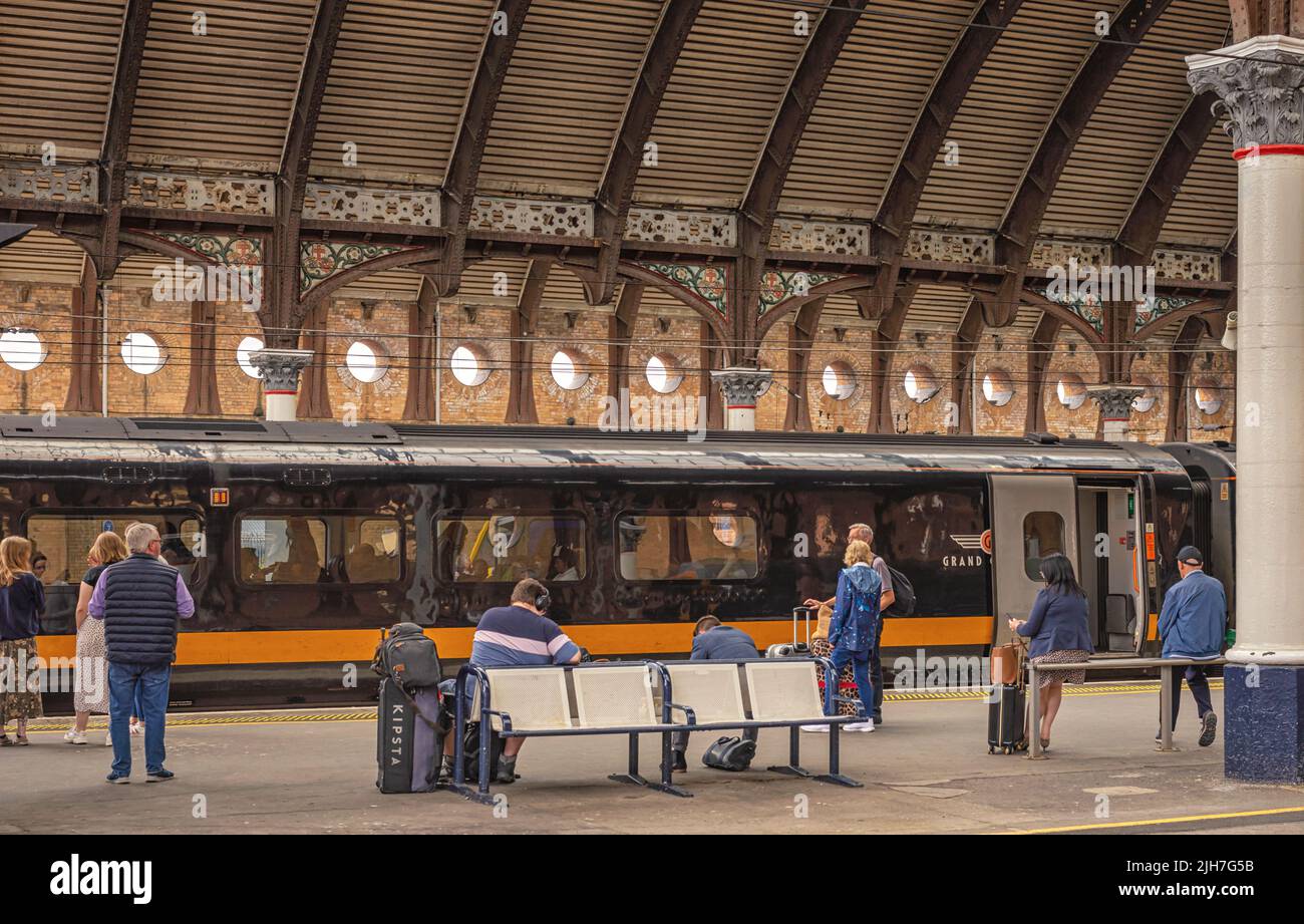 A train rests at a railway station platform under a historic curved ...