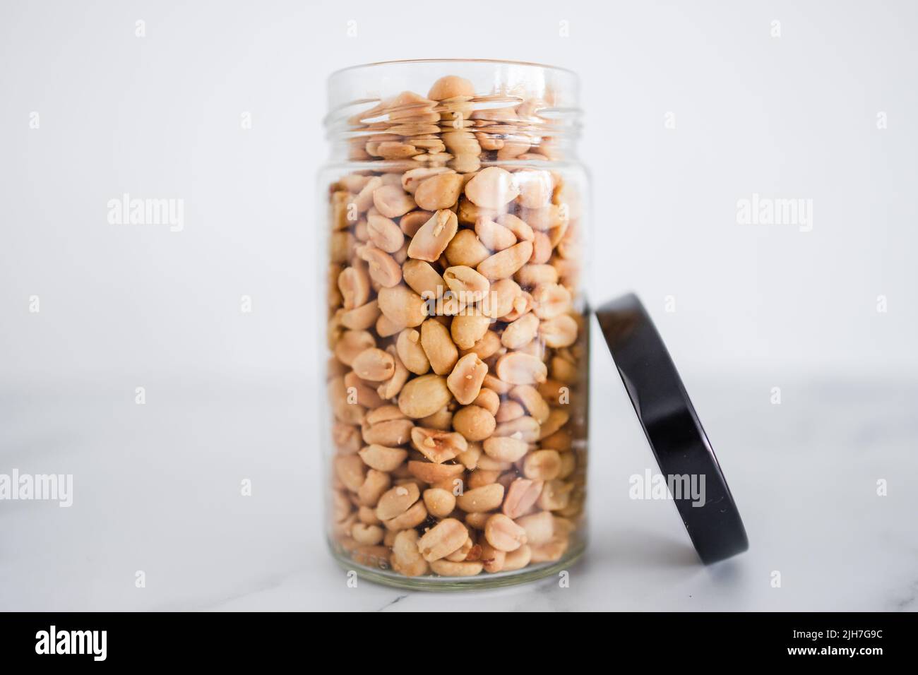 glass jar of peanuts on white marble background, natural healthy pantry ...
