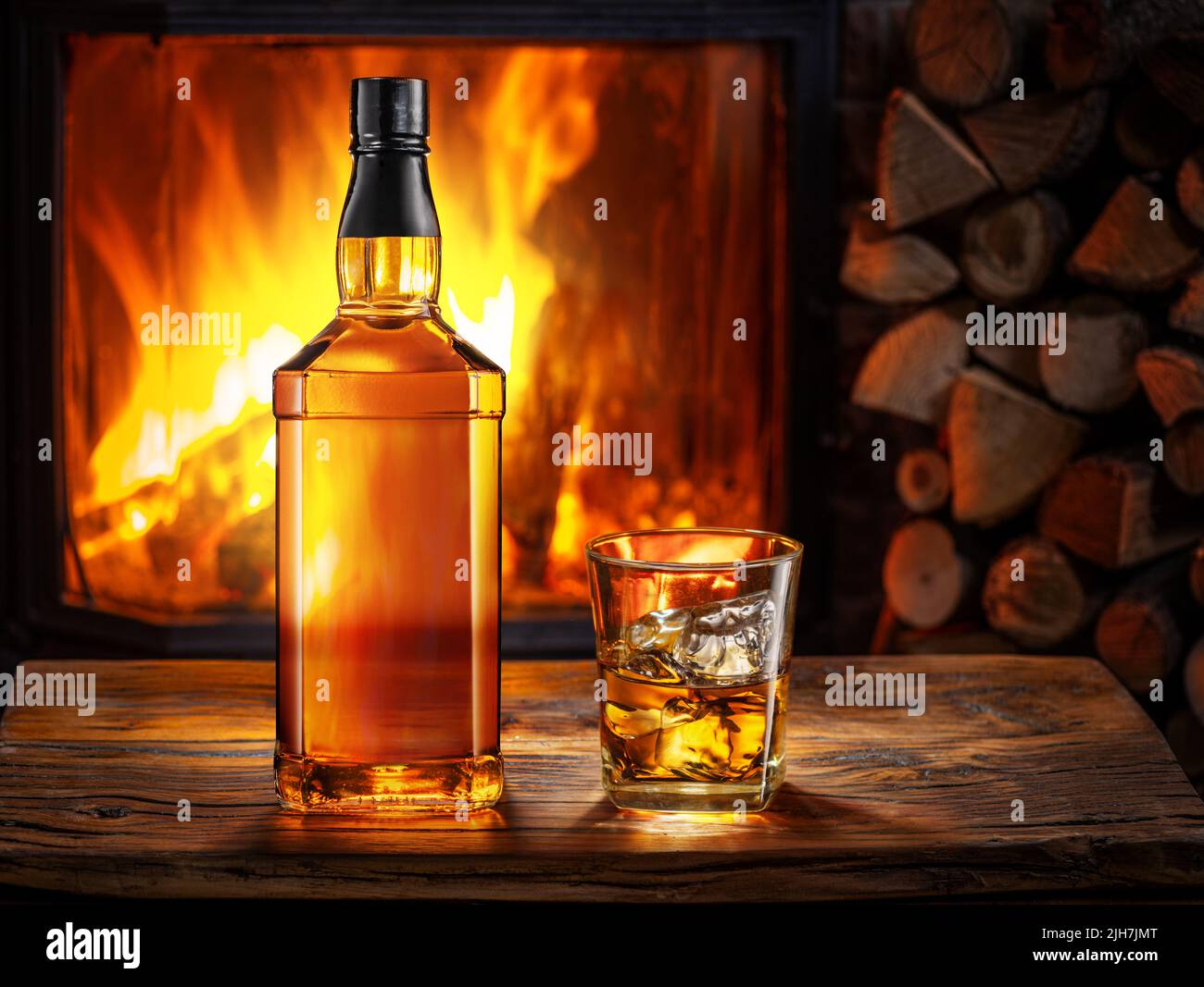 Bottle of whiskey and glass of whiskey with ice. Burning fire in the ...