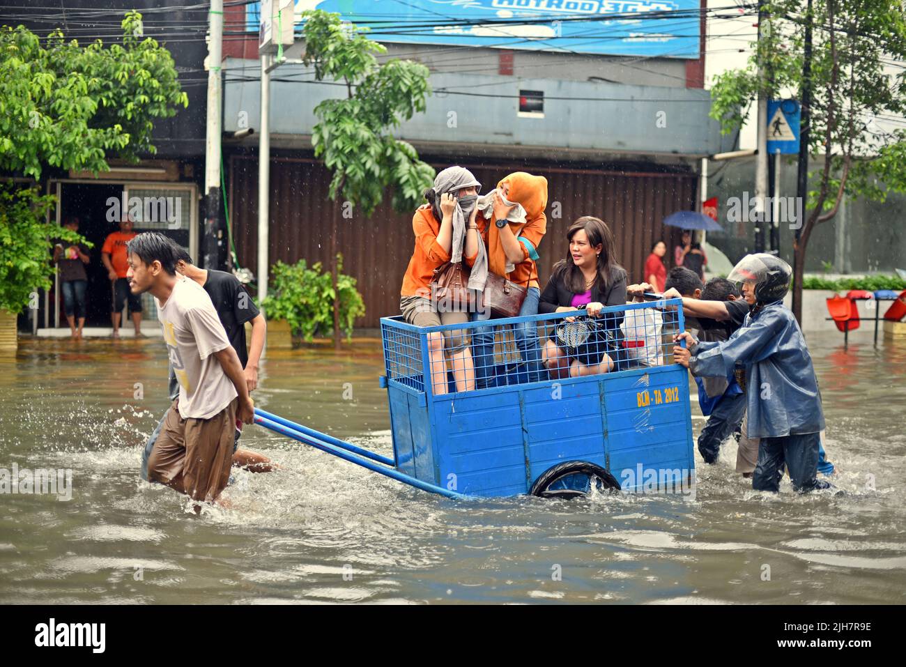 Men helping women to travel through a flooded street by a cart in ...