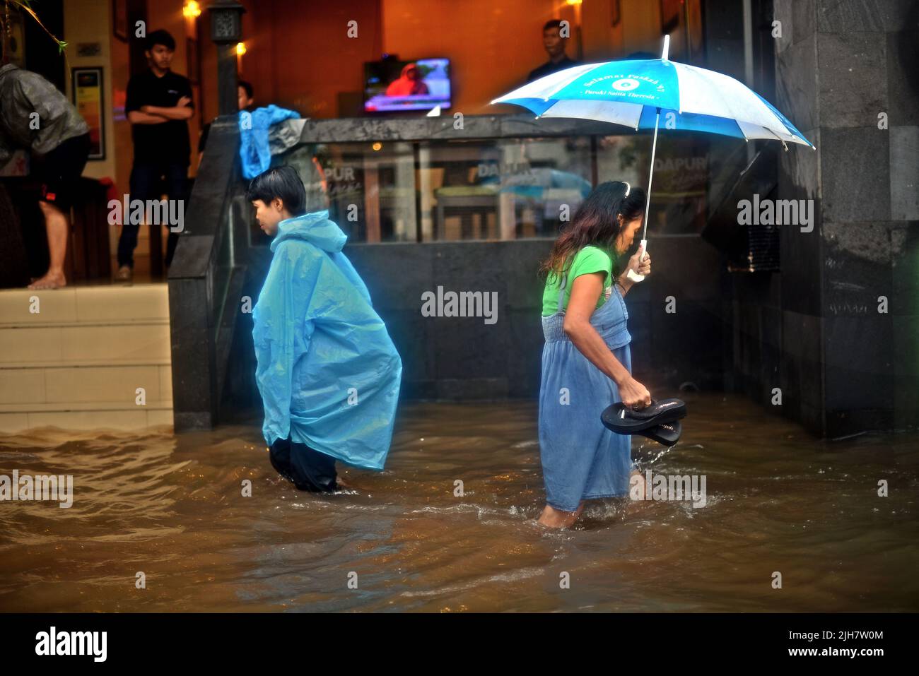 People walking through floodwater on the walkway of a commercial street ...