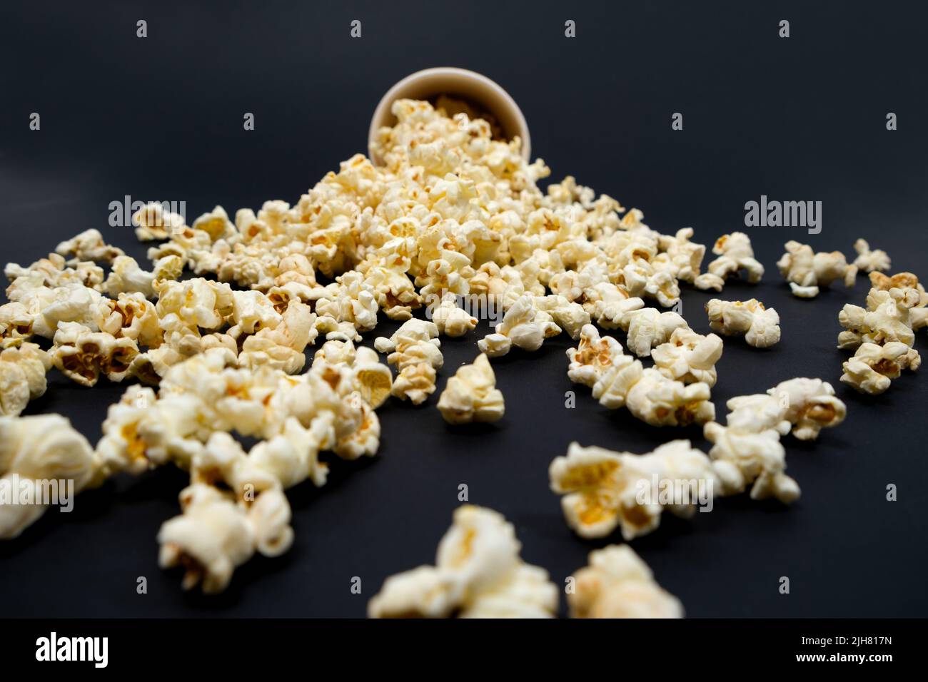 Popcorn spills out of a brown paper cup on a black background close-up ...