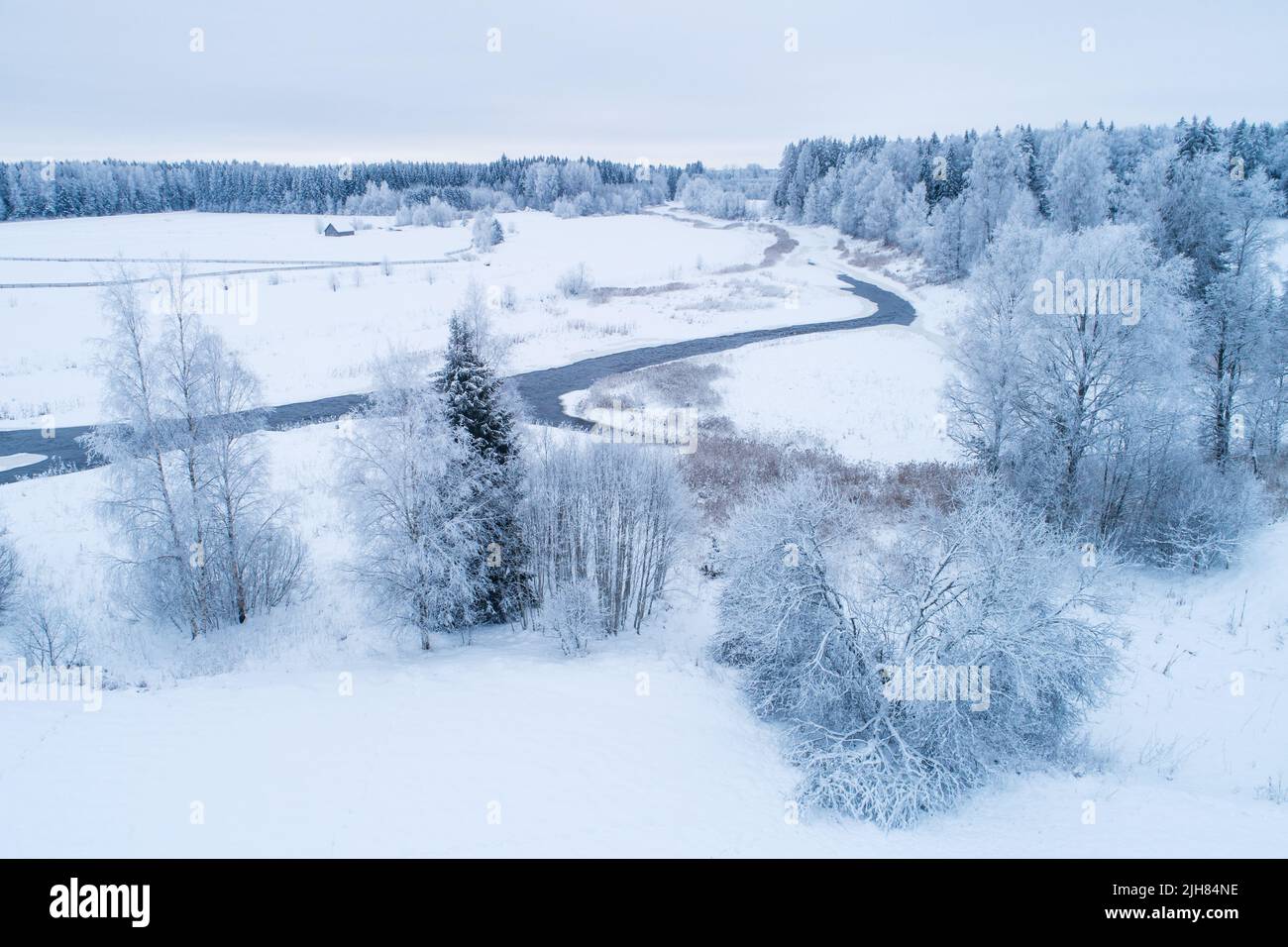 Aerial of a frosty and snowy rural landscape with a open river in Estonian winter, Northern ...