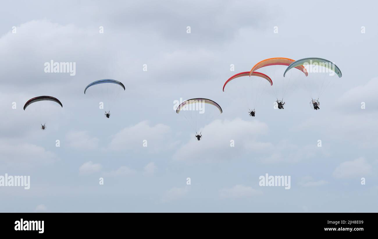 A group of colorful powered paragliders flying in the blue sky with ...