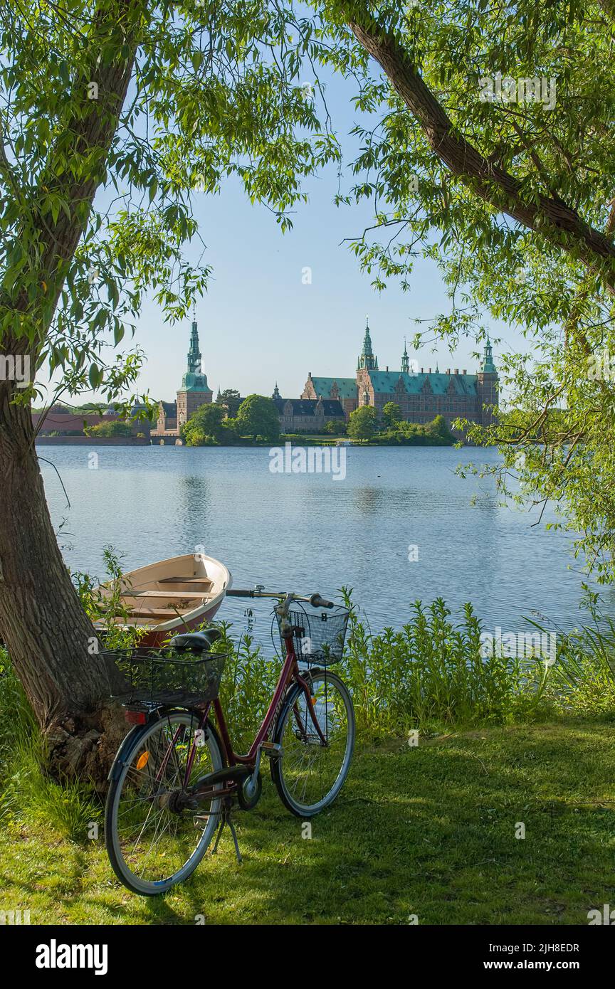 A vertical shot of a bicycle on the shore of a lake with Frederiksborg ...