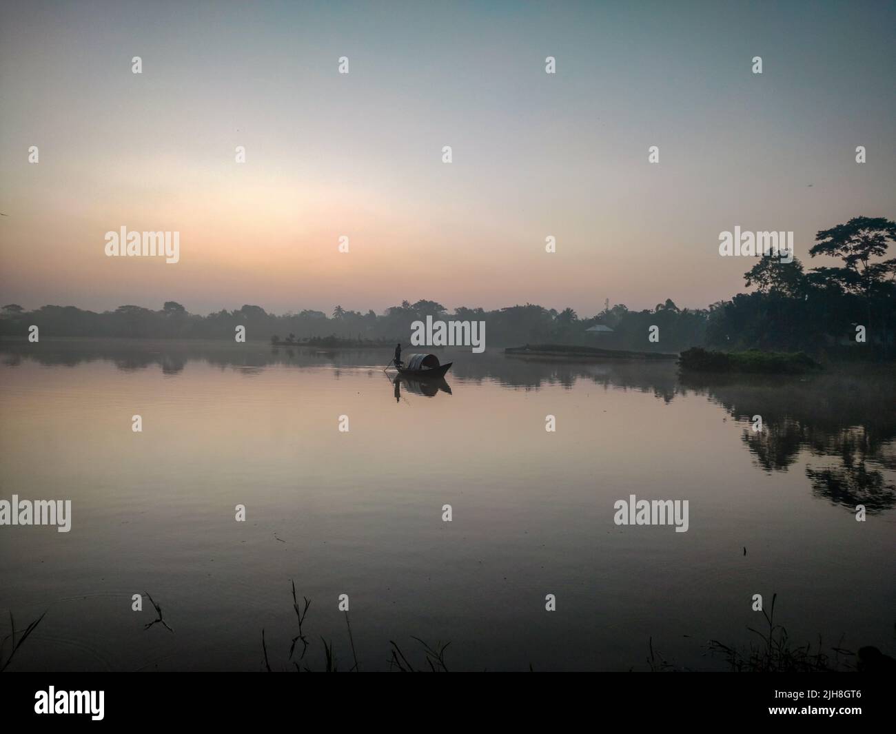 A misty river with a man in an old rowing boat surrounded by trees ...