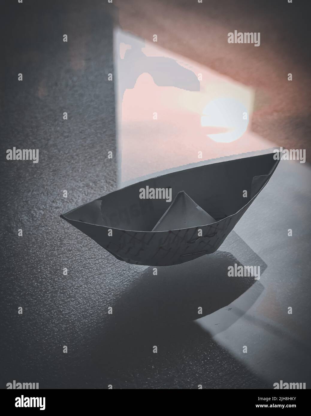 A vertical shot of an origami paper boat floating on water surface with ...