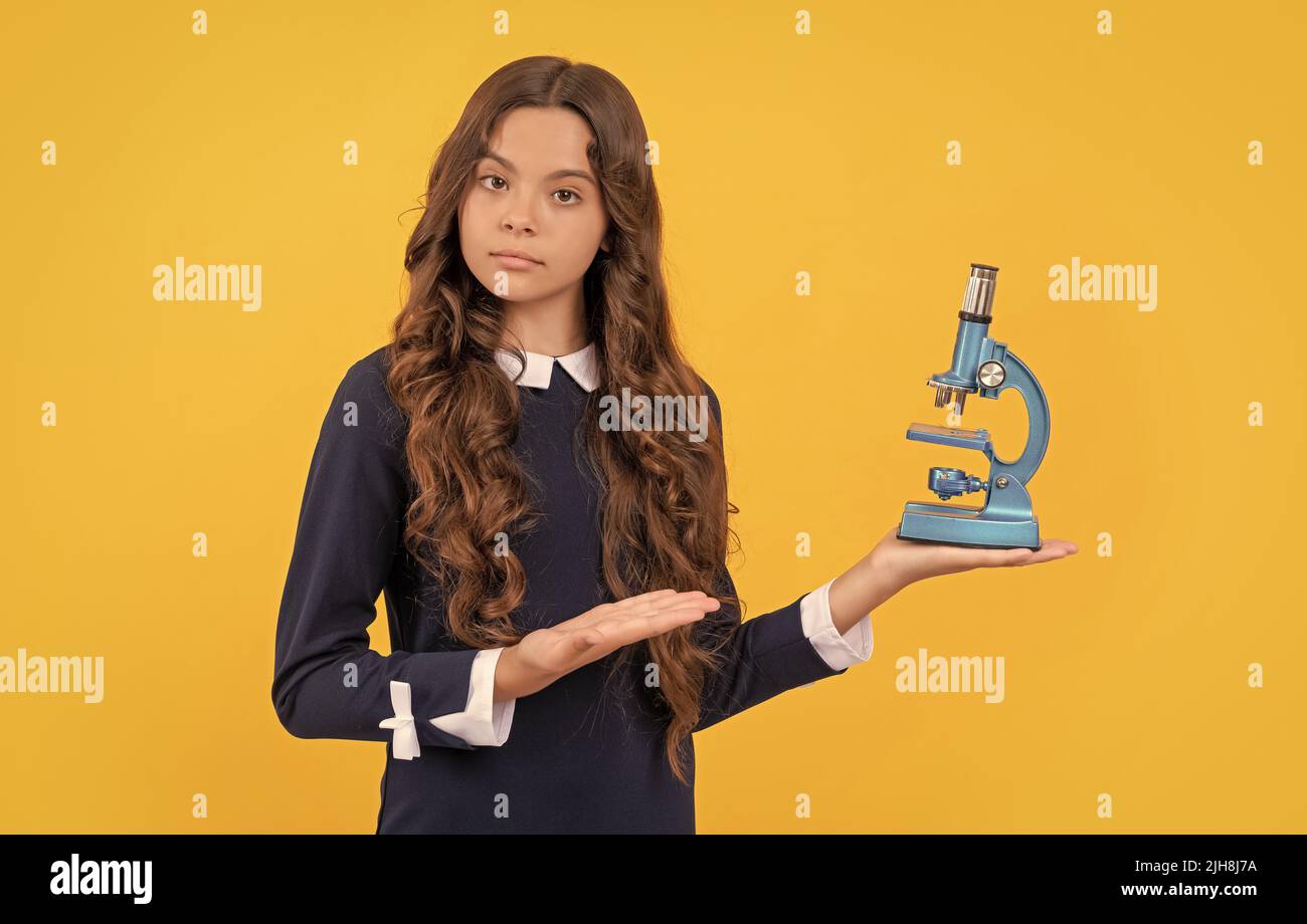 serious nerd child presenting microscope for school education on yellow ...