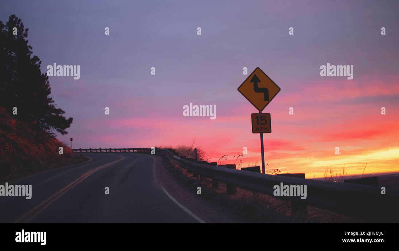 A road sign pole on a curved highway with pink sunset in the background ...