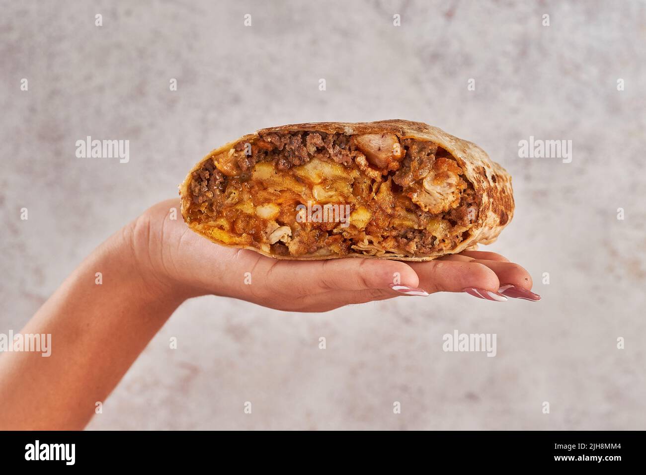 A female hand holding fresh tasty burrito on a blurred background of a ...