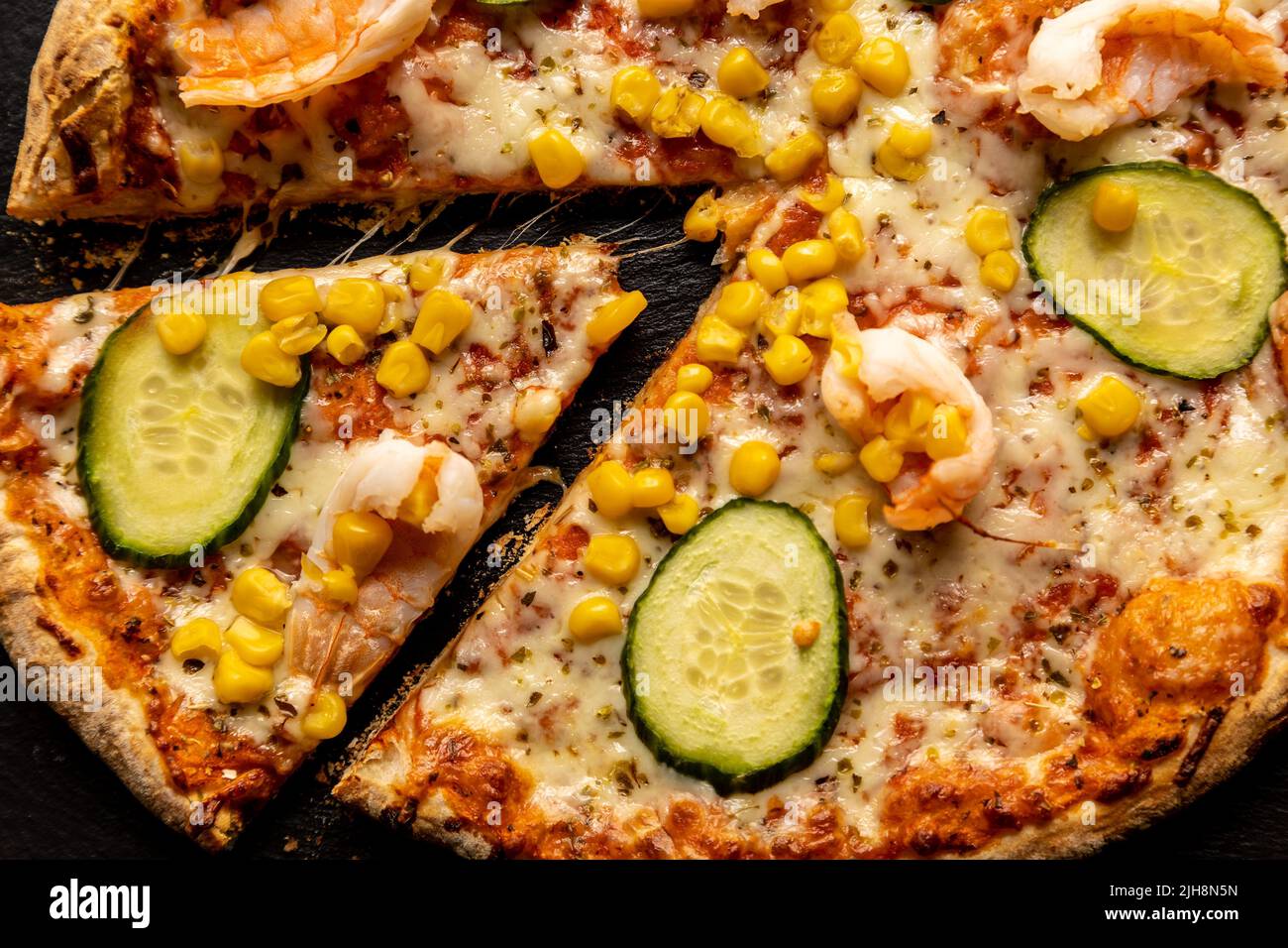 A top view shot of a round pizza topped with cucumbers, corn and shrimp ...
