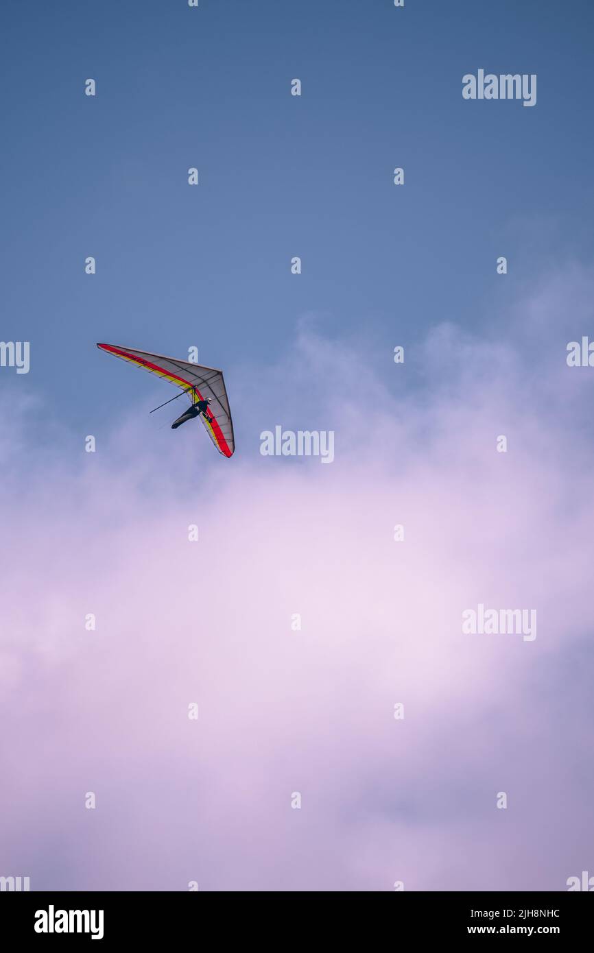 A vertical shot of a hang glider with red line in the blue sky with a ...