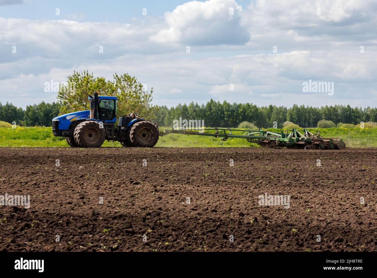 Blue tractor with double wheels pulling disc harrow with roller basket ...