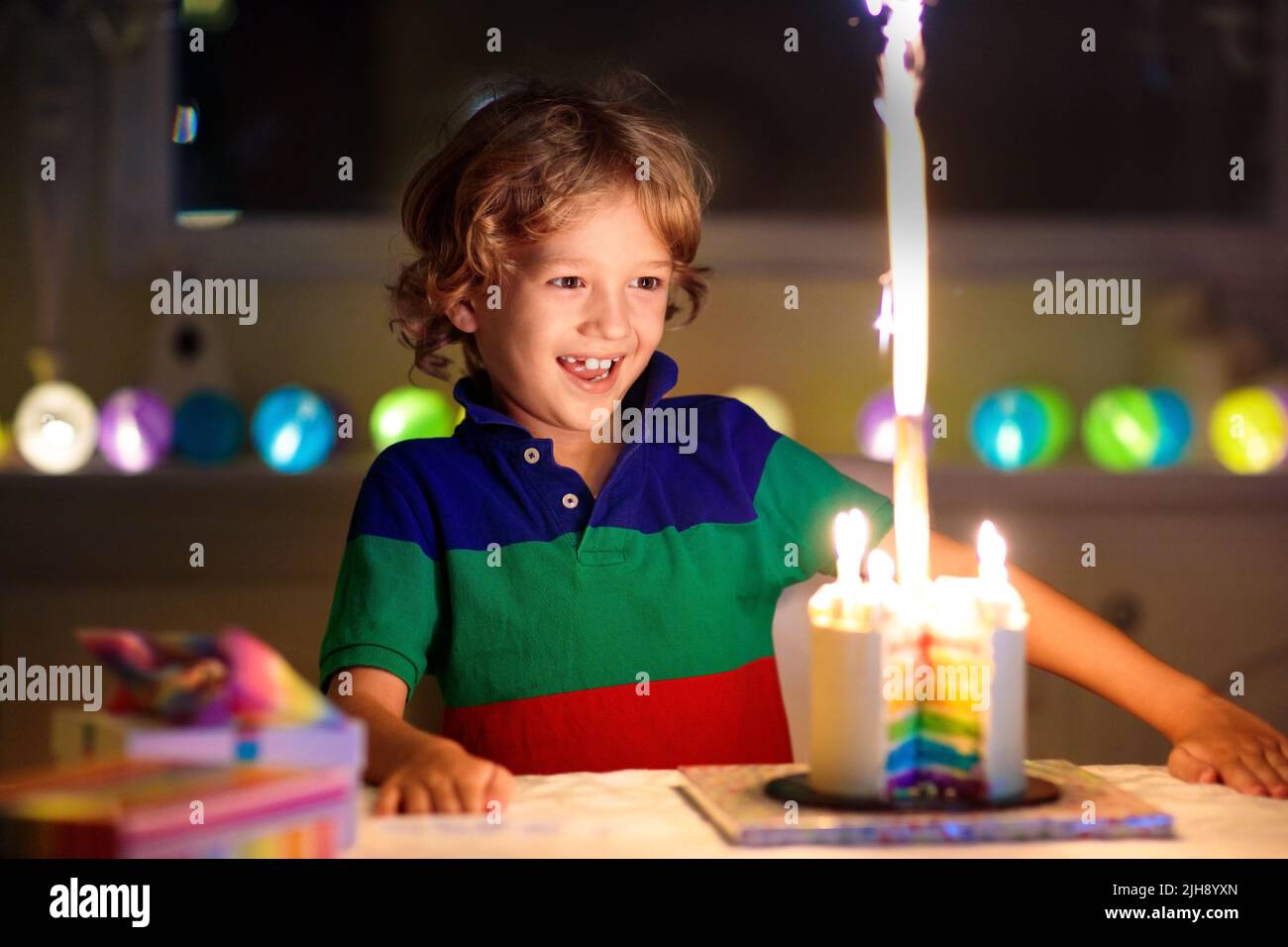 Kids birthday party. Child blowing candles on cake and opening presents ...