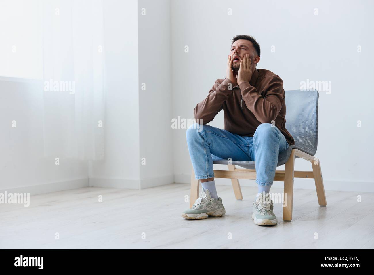 Sleepy tired upset unhappy young man touch head both hands closes eyes ...