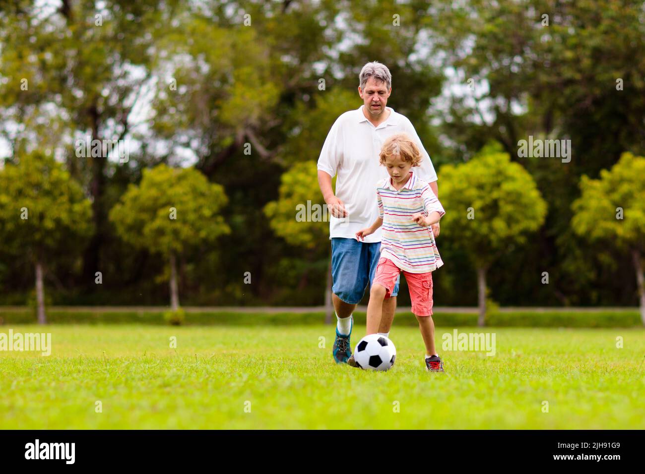 Father and son play football on outdoor pitch. Dad and kid run on park ...