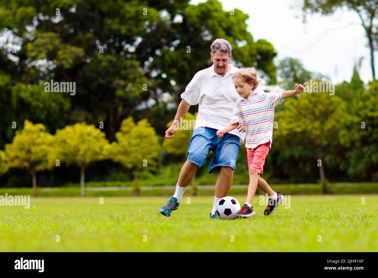 Father and son play football on outdoor pitch. Dad and kid run on park ...
