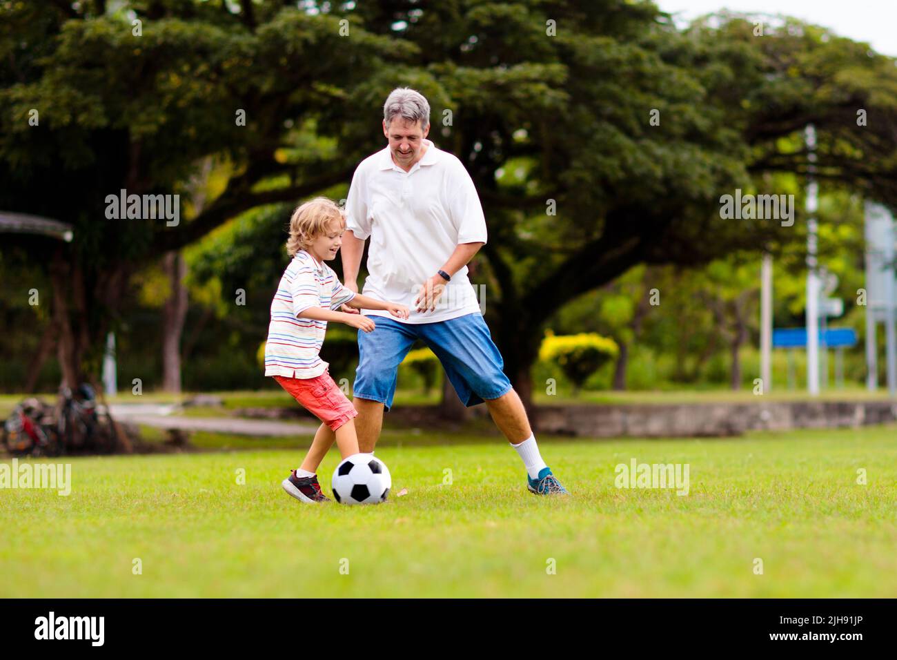 Father and son play football on outdoor pitch. Dad and kid run on park ...