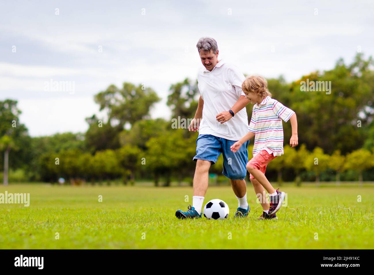 Father and son play football on outdoor pitch. Dad and kid run on park ...