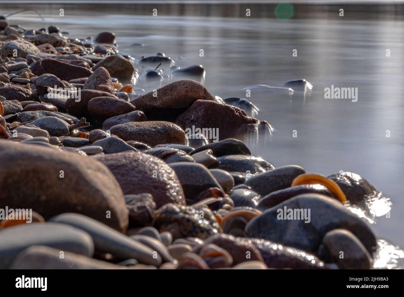 A closeup shot of wet pebbles on the coast of a lak Stock Photo - Alamy