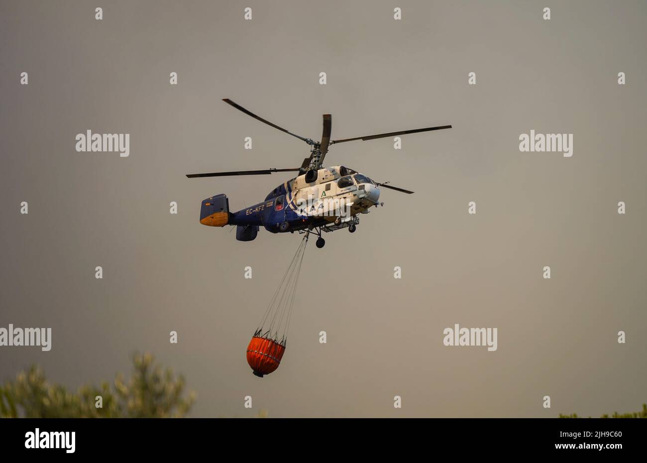 Heavy helicopter of INFOCA carrying a water bucket to drop on a ...