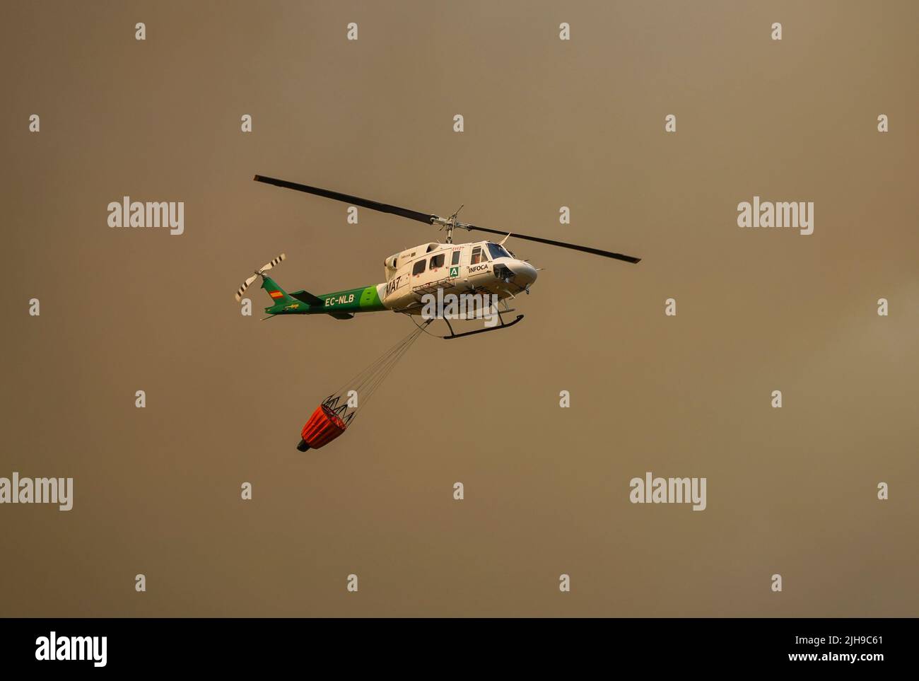 Medium sized helicopter of INFOCA carrying a water bucket to drop on a ...