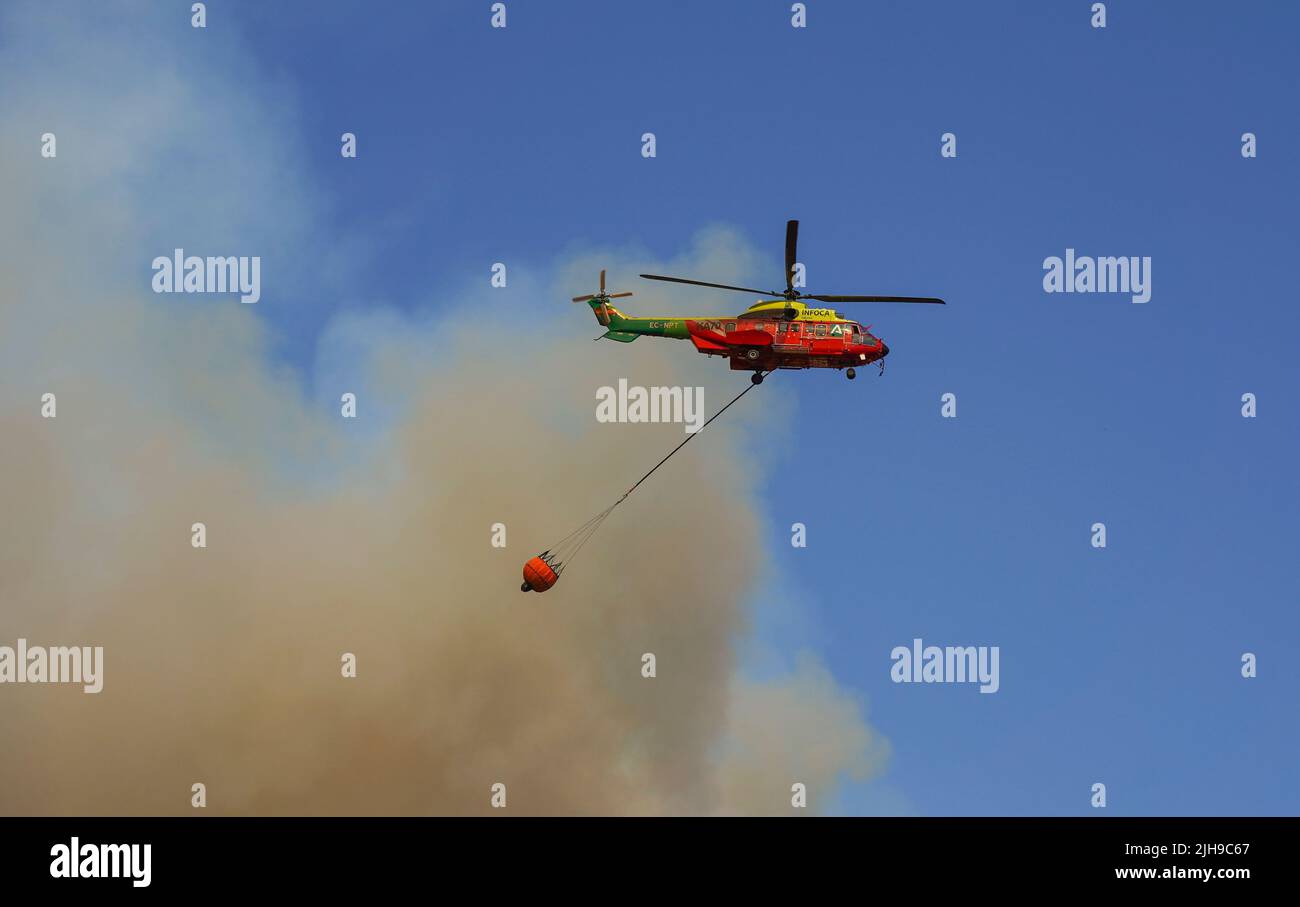 Medium sized helicopter of INFOCA carrying a water bucket to drop on a ...