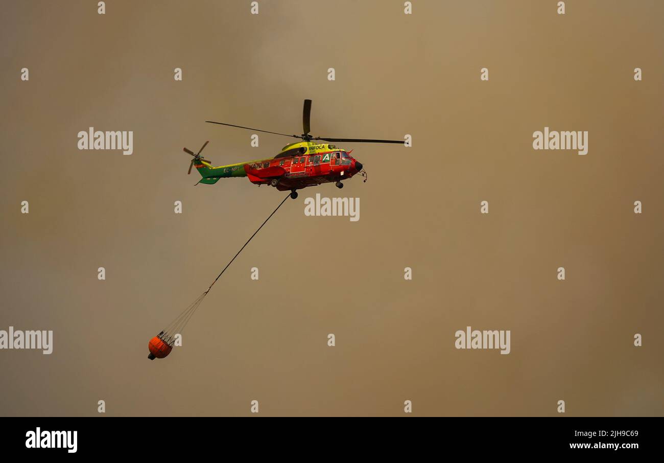 Medium sized helicopter of INFOCA carrying a water bucket to drop on a ...