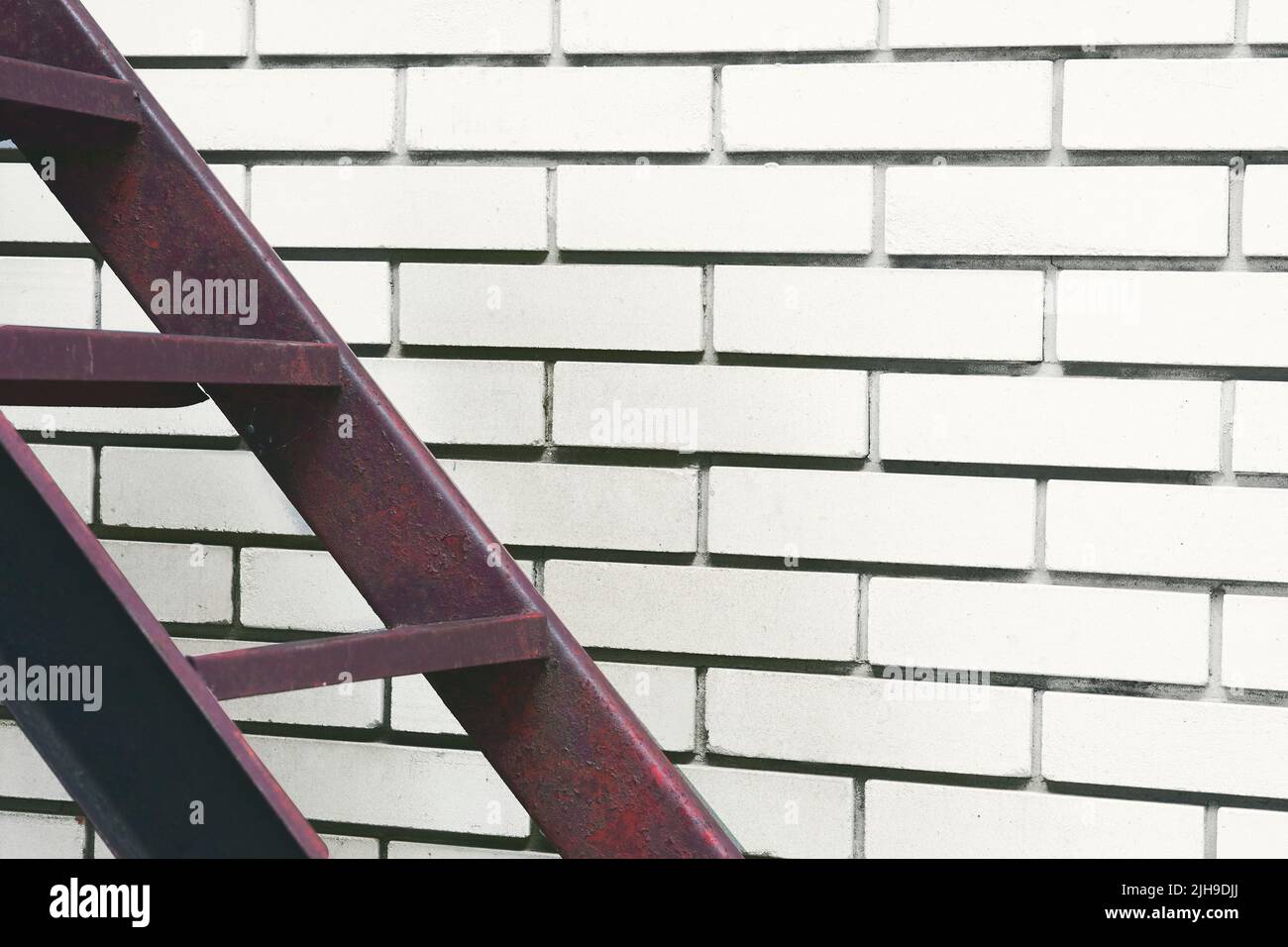 Part of the stairs red metal ladder leading up against of a white brick ...