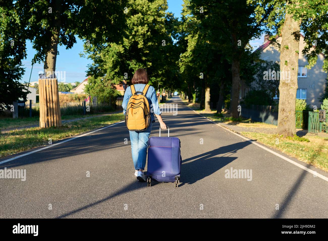 Woman walking on road in street with suitcase and backpack, back view ...