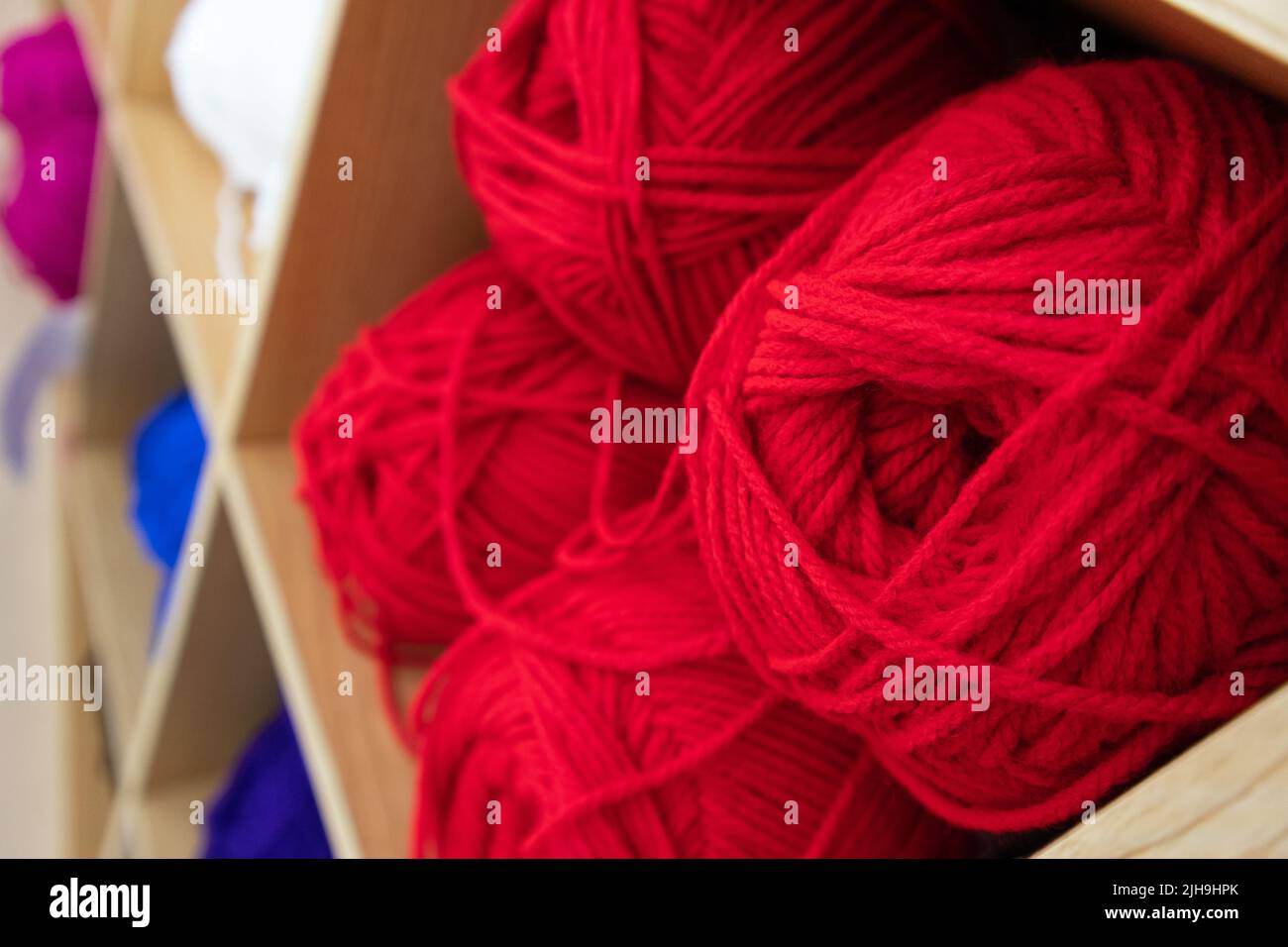 close up stack of colorful red worsted wool yarn batch in square spaces ...