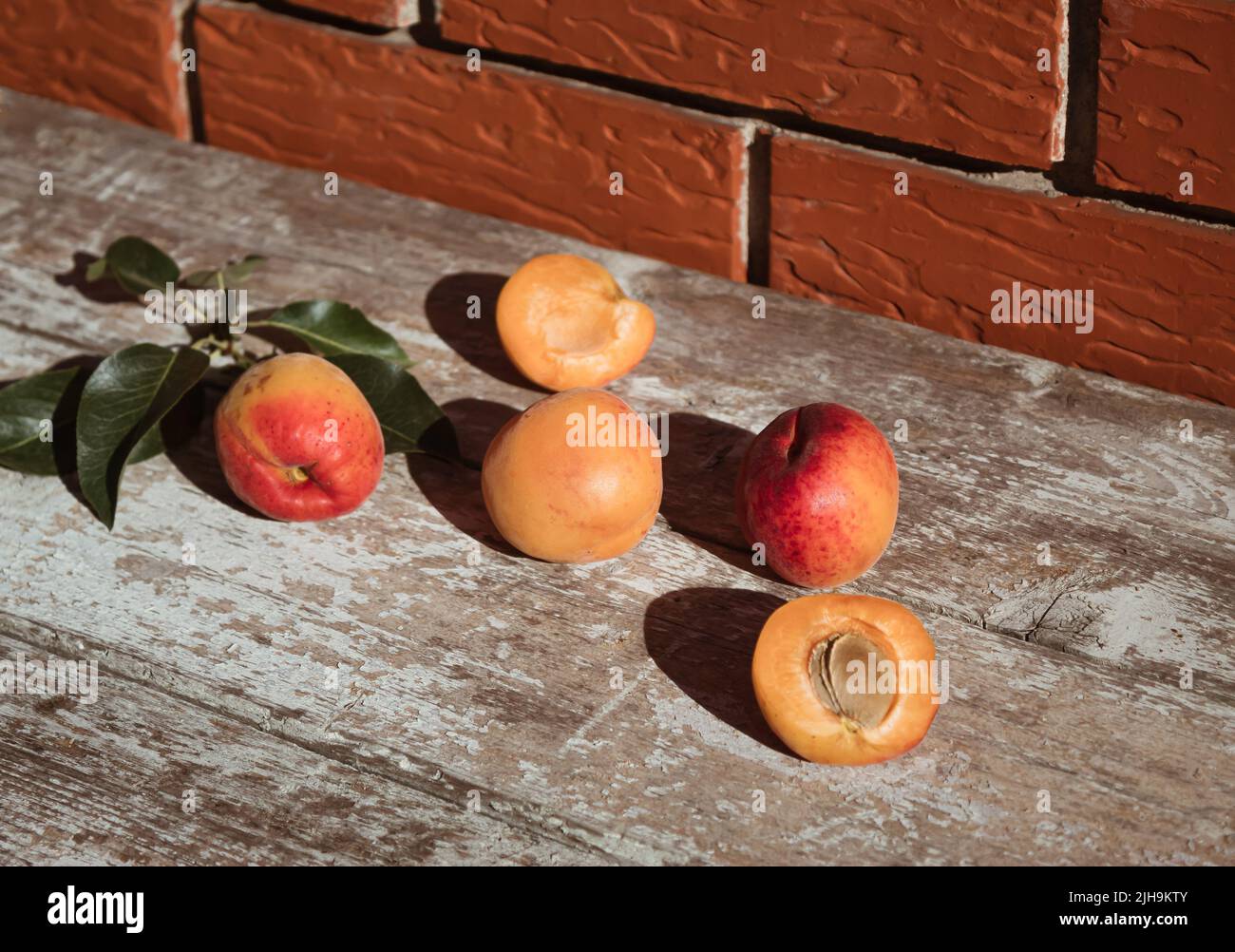 Summer scene with fresh apricots on wooden table and brick background ...