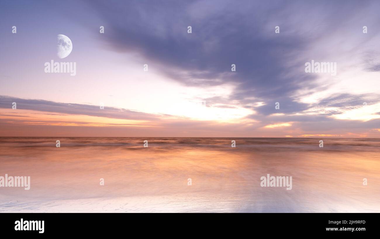 View of the moon rising over the sea with a cloudy sky above the ...