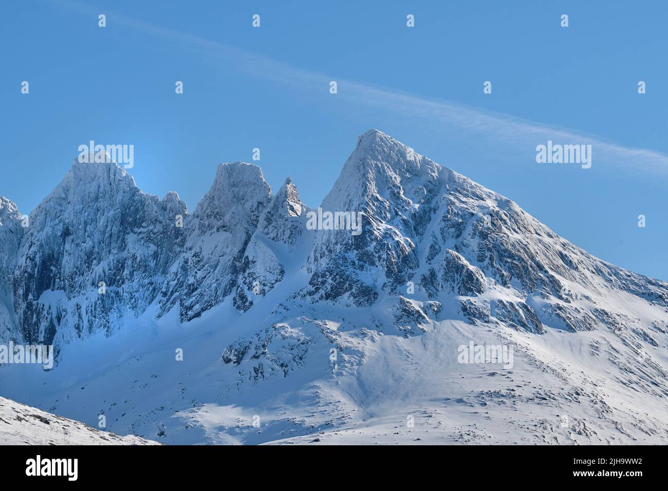 A cold mountain peak covered in snow during winter with a blue sky ...