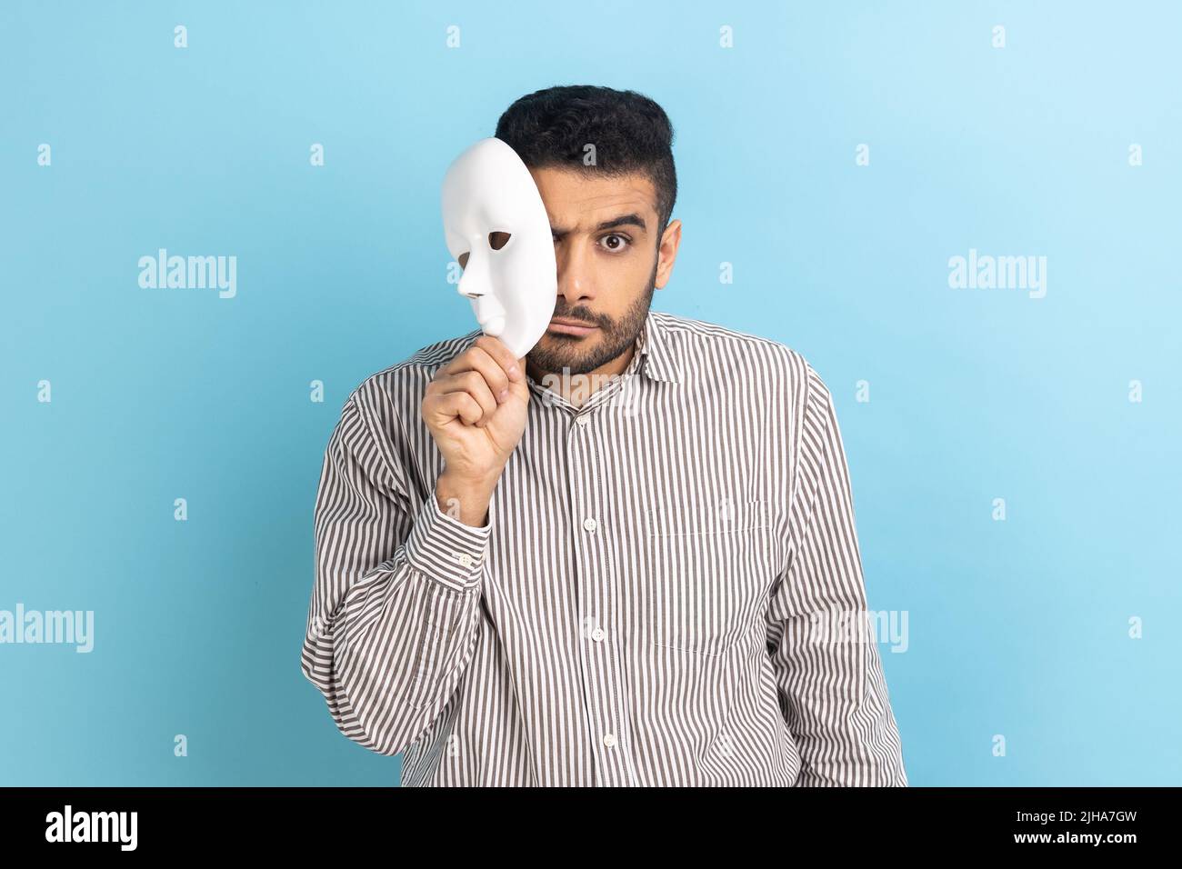 Serious bearded businessman removing white mask from face showing his ...