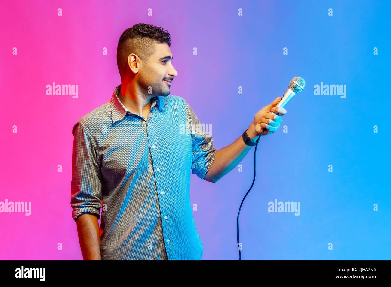 Side view of attractive man in shirt posing with microphone in hands ...